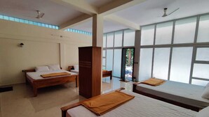 Quarto de hotel com duas camas, guarda-roupa de madeira e janelas amplas com painéis de vidro jateado.