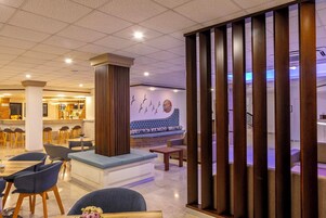 Um saguão de hotel moderno com área de estar, um bar e uma parede decorativa com um mural de pássaros.