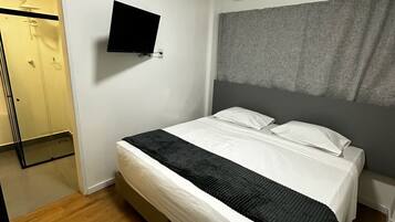 Quarto de hotel com cama, televisão na parede, ar condicionado e porta para um banheiro.