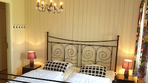 Uma cama com estrutura de metal, duas mesas de cabeceira com abajures, um candelabro e uma parede de madeira com uma porta.