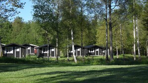Fileira de cabanas numa área arborizada, com um trilho de terra a caminho.