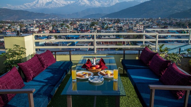 Terraço com mesa posta para o café da manhã, com vista para uma cidade e montanhas.