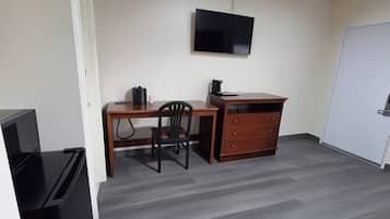 Um quarto pequeno com escrivaninha, cadeira, televisão fixada na parede, armário e porta branca.