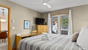 Quarto com cama, escrivaninha, cadeira, televisão e vista para o exterior.