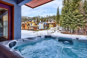 Uma banheira de hidromassagem com vista para casas coloridas e terreno coberto de neve.