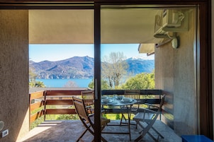 Varanda com mesa e cadeiras, vista para uma paisagem montanhosa e um corpo d'água.