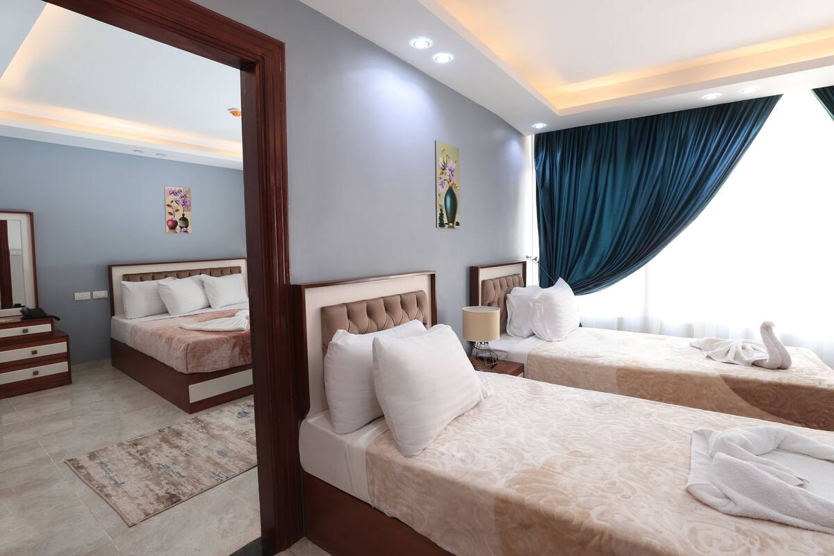 Quarto de hotel com duas camas, um espelho grande, mesa de cabeceira, abajur e janela com cortinas.