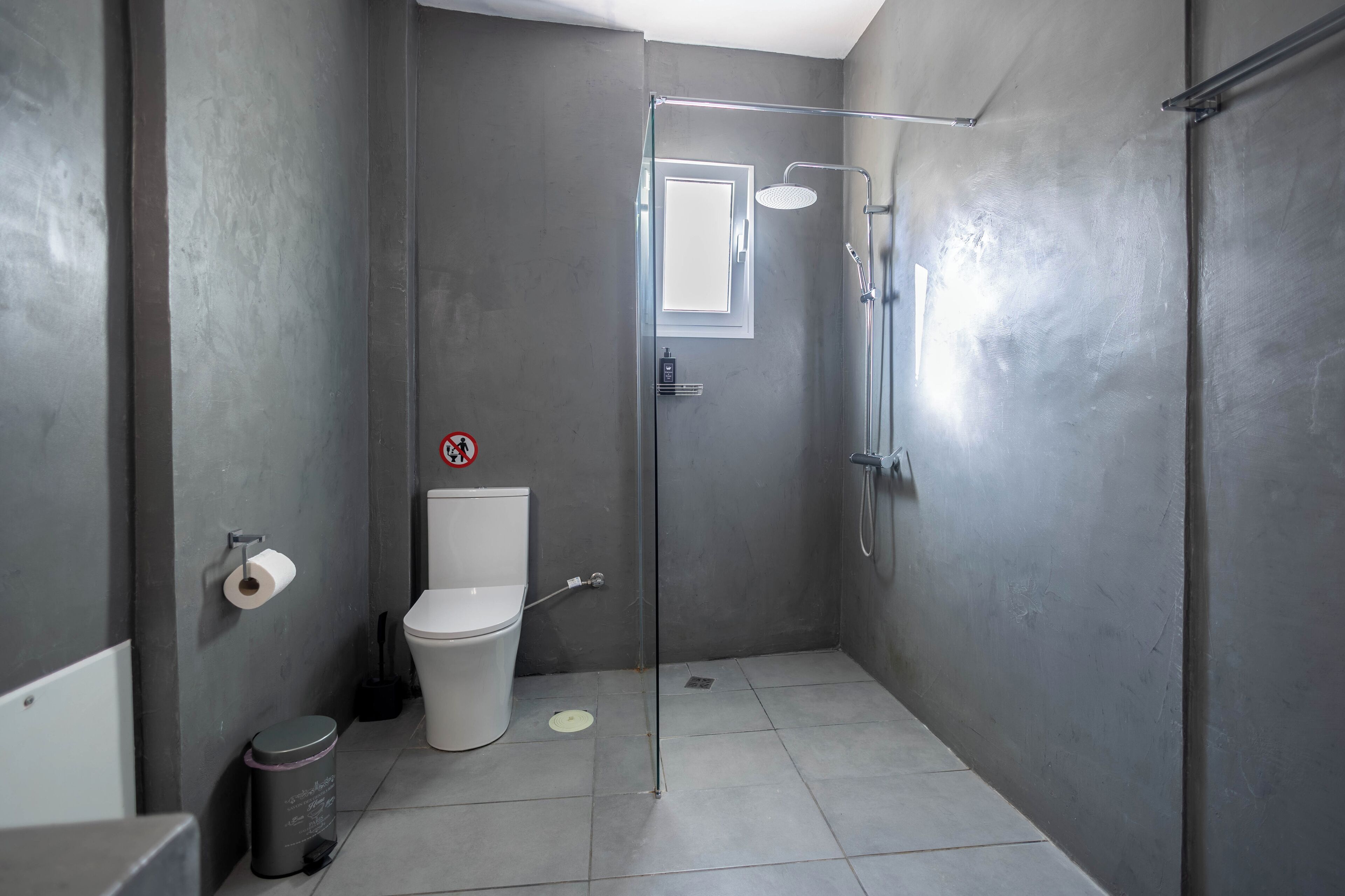 Um banheiro moderno com chuveiro em box de vidro, vaso sanitário e lixeira.