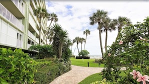 Um hotel com um caminho que leva a uma área gramada, palmeiras e vista para o oceano.