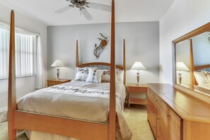 Uma cama com dossel e estrutura de madeira, duas mesas de cabeceira com abajures, um espelho grande e uma obra de arte pendurada na parede.