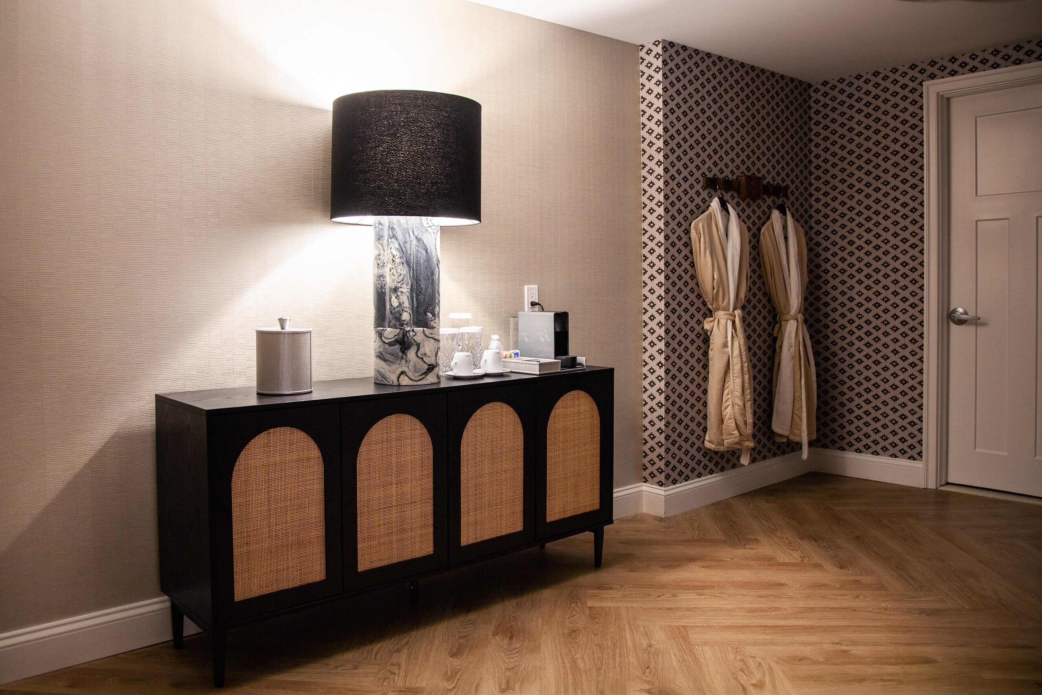 Quarto de canto com uma mesa consola de madeira escura, uma luminária de mármore e papel de parede estampado.