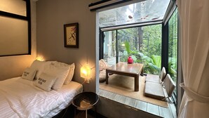 Quarto moderno com cama, mesa de cabeceira e janela com vista para o verde.