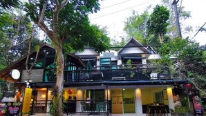 Um edifício de dois andares com varanda, área de refeições com mesas ao ar livre e placa de restaurante.