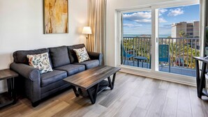 Uma sala de estar com sofá, mesa de centro e uma janela grande com vista para o mar e prédios.