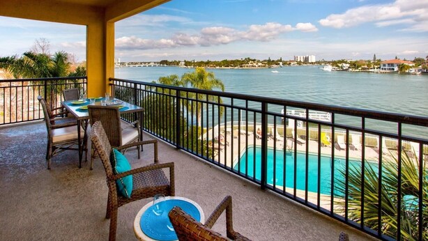 Varanda com móveis de vime, uma mesa de jantar e vista para uma piscina e rio.