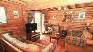 Interior acolhedor de uma cabana de madeira com um sofá de couro, um sofá estampado em xadrez, uma televisão e uma lareira.