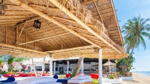 Um resort à beira-mar com construções de palha, espreguiçadeiras e uma palmeira.