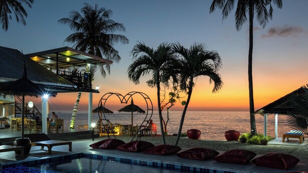Uma área à beira da piscina com vista para o oceano ao pôr do sol, cadeiras de descanso e um restaurante chamado El Pillax Lanta Resort Restaurant.