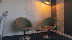 Duas poltronas modernas com design acolchoado, uma mesinha e um candeeiro de chão numa sala com papel de parede e tapete estampados.
