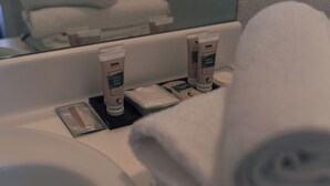 Artigos de higiene em uma casa de banho de hotel, incluindo gel de cabelo e corpo, e uma toalha.