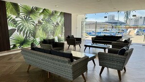 Uma área de estar moderna com móveis de vime, uma mesa de centro de vidro e vista para a área da piscina.