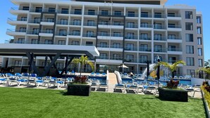 Hotel de vários andares com área de piscina, espreguiçadeiras e palmeiras.