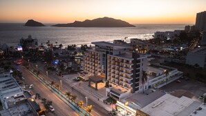 Um hotel moderno com vários andares, piscina no terraço e vista para o oceano ao pôr do sol.