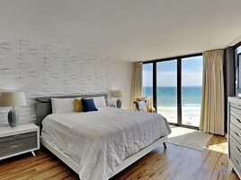 Quarto moderno com uma cama grande, mesas de cabeceira e vista para o oceano.