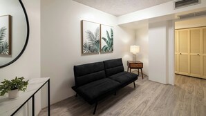 Um interior moderno com um sofá preto, um espelho redondo e duas gravuras botânicas emolduradas na parede.