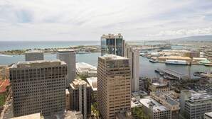 Um edifício alto com fachada de vidro moderna, rodeado por outros edifícios comerciais, uma marina com barcos e uma vista desobstruída da costa.