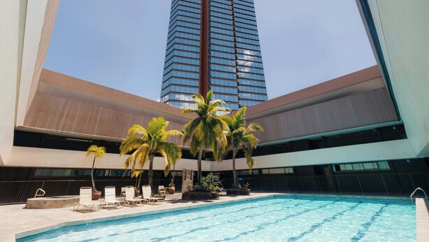 Um edifício moderno com piscina, palmeiras e céu claro.