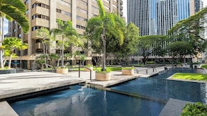 Um edifício moderno com área de piscina, rodeado por vegetação e um céu limpo.