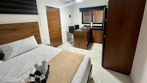 Quarto de hotel com cama, escrivaninha e cozinha compacta.