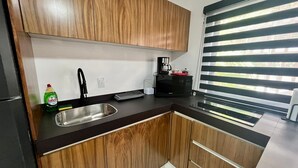 Uma cozinha moderna com armários de madeira, uma pia de aço inoxidável, um micro-ondas preto e uma janela com persianas.