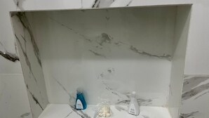 Casa de banho com toucador de mármore e prateleira com frasco de champô e frasco de loção.