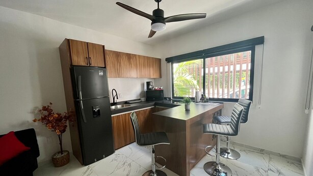 Uma cozinha compacta com geladeira, pia e banquetas.