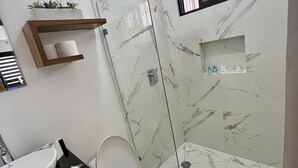 Casa de banho moderna com chuveiro de mármore branco, sanita e lavatório.