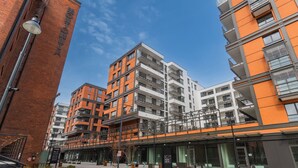 Um edifício com várias andares, fachadas em tons de laranja e branco, uma entrada visível e um céu claro.
