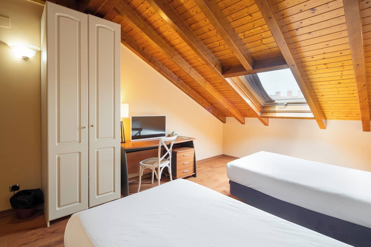 Quarto com teto inclinado, uma escrivaninha com cadeira, uma cama e um guarda-roupa.