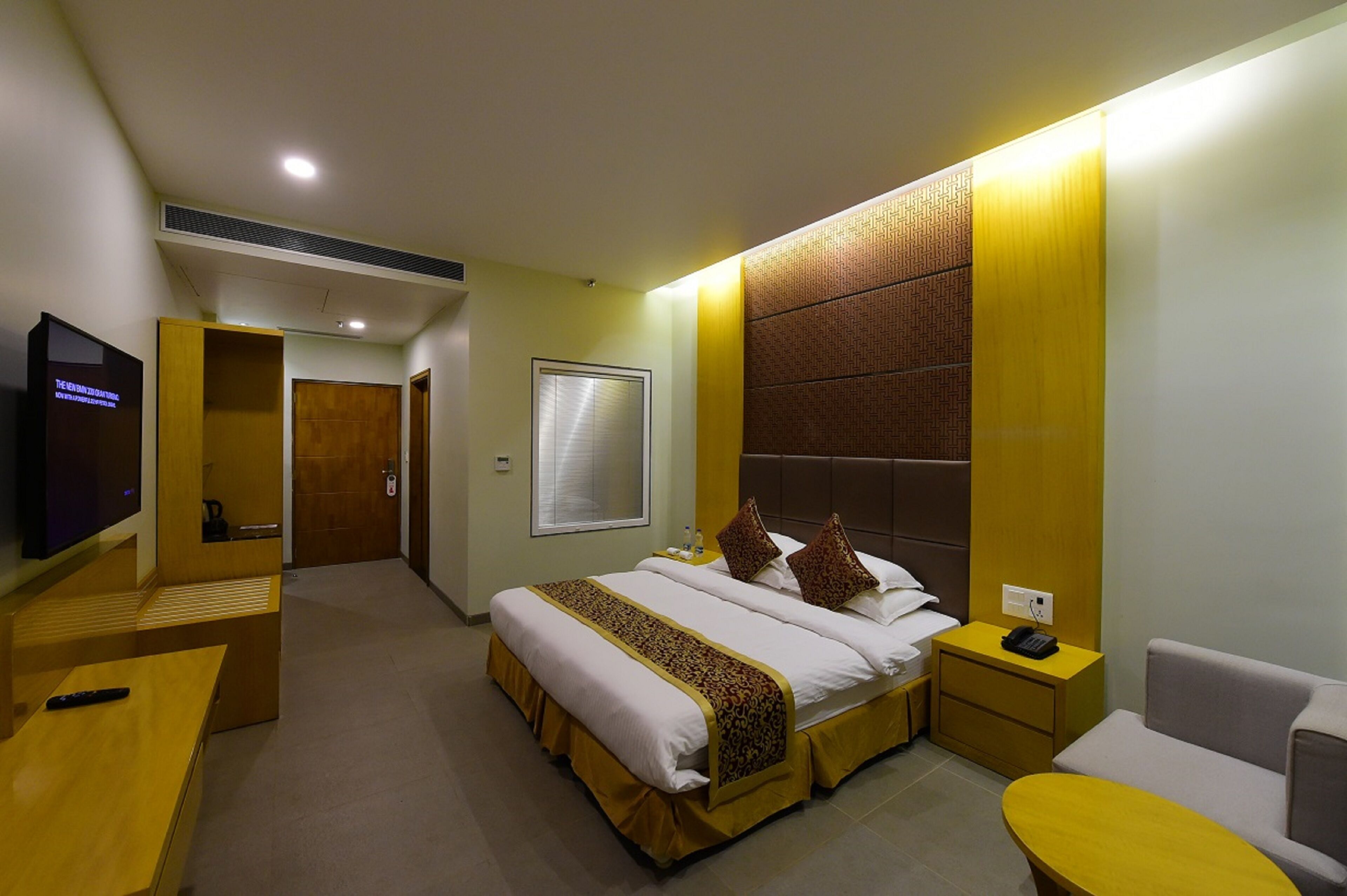 Quarto de hotel com uma cama grande, mesas de cabeceira, televisão e um espaço de estar.