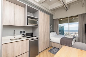 Quarto de hotel moderno com cozinha compacta, cama com vista e uma janela grande.