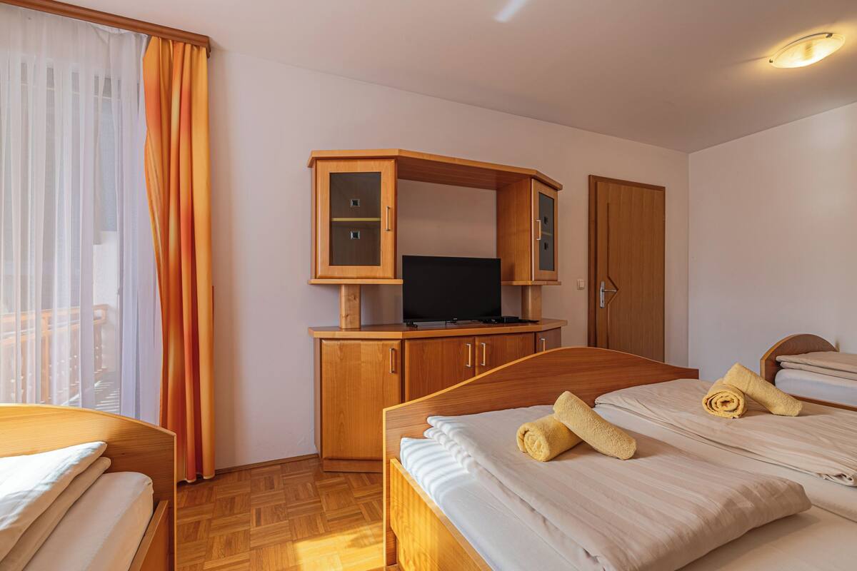 Quarto de hotel com duas camas, uma escrivaninha de madeira com televisão e uma janela com cortinas.