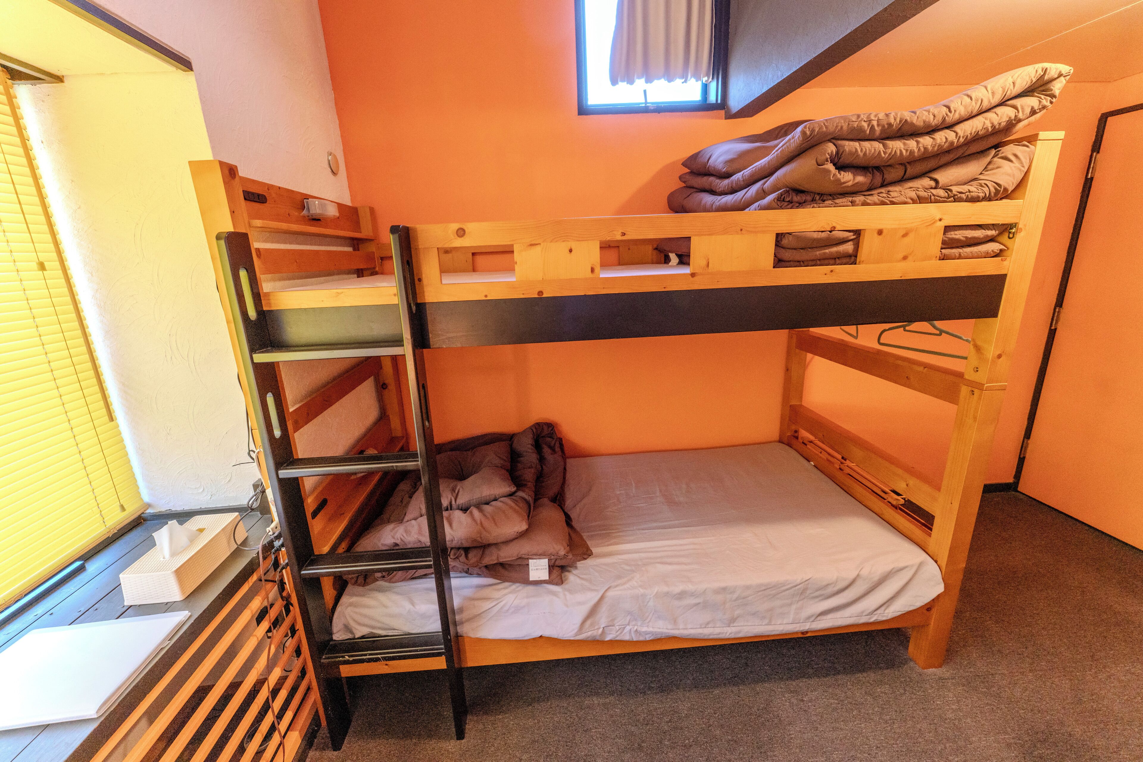Uma cama beliche com escada, uma janela com cortinas e um radiador.