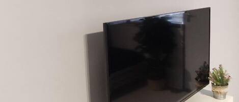 Uma sala de estar moderna com uma TV de tela plana fixada em uma parede branca, um console branco abaixo e três decorações circulares pretas na parede.