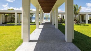 Uma galeria coberta com vista para o oceano, cercada por palmeiras e um céu claro.