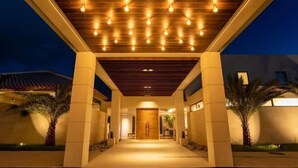 Uma galeria coberta com teto de madeira e luminárias, que leva à entrada de um edifício.