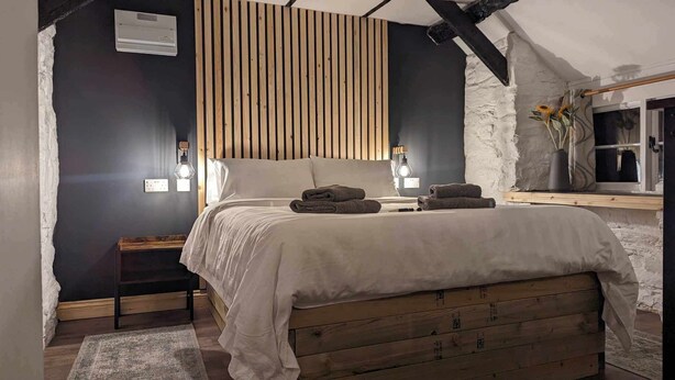 Quarto com cama de madeira, teto inclinado e parede de pedra.