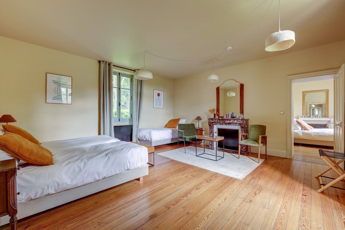 Quarto de hotel com duas camas, lareira, espelho e vista para o exterior.