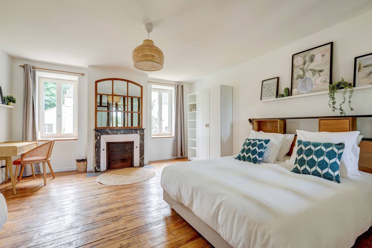 Quarto com uma cama grande, lareira, piso de madeira e escrivaninha com cadeira.