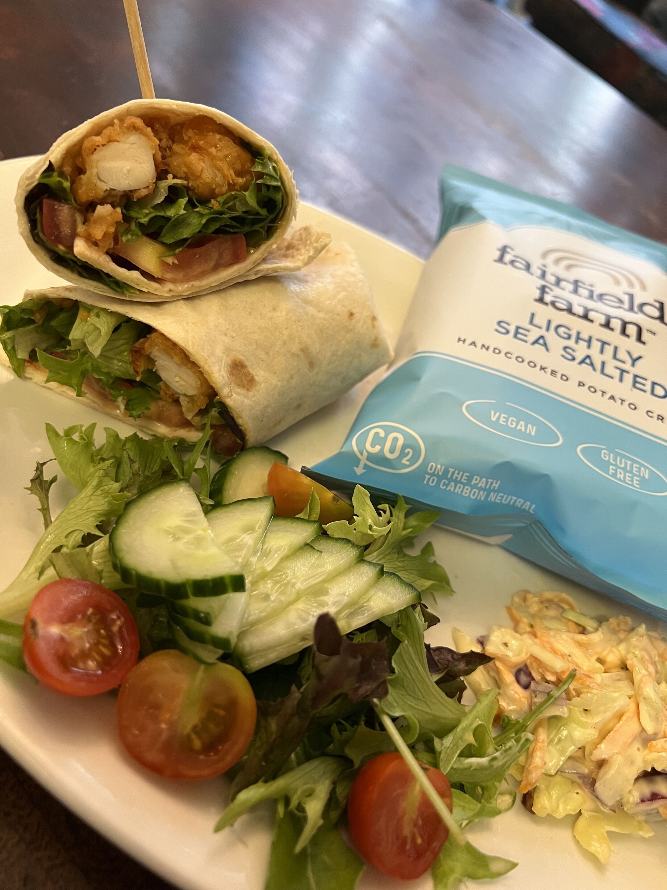 Um prato com um wrap, salada e um saco de batatas fritas Fairfield Farm levemente salgadas.